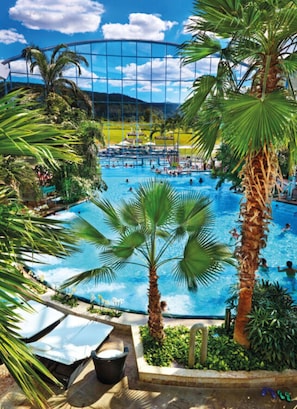 Uma área de piscina com palmeiras, espreguiçadeiras e vista para uma paisagem montanhosa.