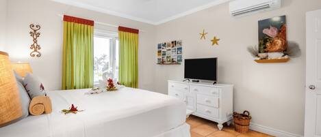 Quarto de hotel com cama, televisão, penteadeira e janela com cortinas.