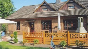 Uma casa de dois andares de tijolo com telhado telhado, chaminé e cerca de madeira.