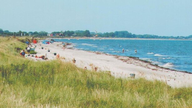 Uma praia com pessoas e tendas, áreas gramadas e céu claro.