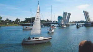 Um veleiro com o número 220 na vela, atracado perto de uma ponte com design único.