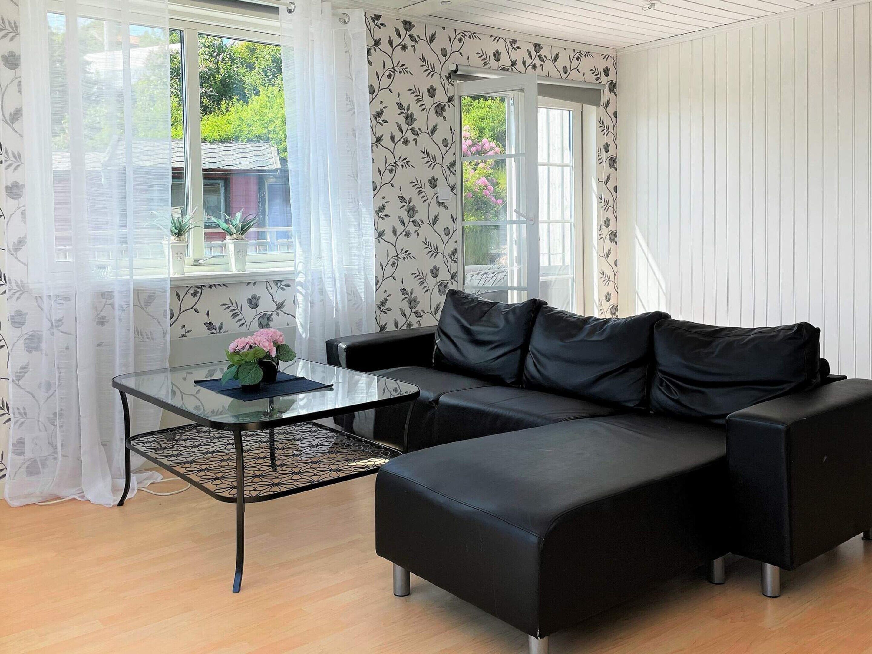 Uma sala de estar moderna com sofá seccional, mesa de centro de vidro e papel de parede estampado com flores.