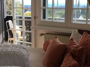 Quarto com uma janela grande, cama com roupa de cama branca e vista para o exterior.