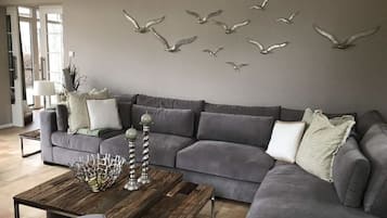 Uma sala de estar moderna com um sofá modular cinza, uma mesa de centro de madeira e arte de parede com tema de pássaros.