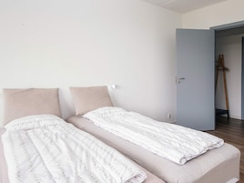Quarto com duas camas, uma porta que dá para outro espaço e um cavalete de madeira no canto.
