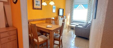 Uma área de jantar com uma mesa e cadeiras de madeira, uma televisão e um sofá ao fundo.