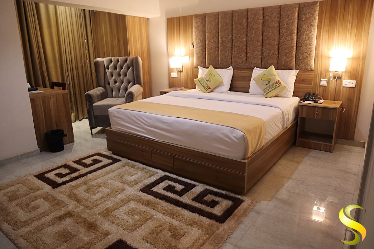 Quarto de hotel com uma cama grande, uma cadeira, uma escrivaninha e uma mesa de cabeceira com abajur.