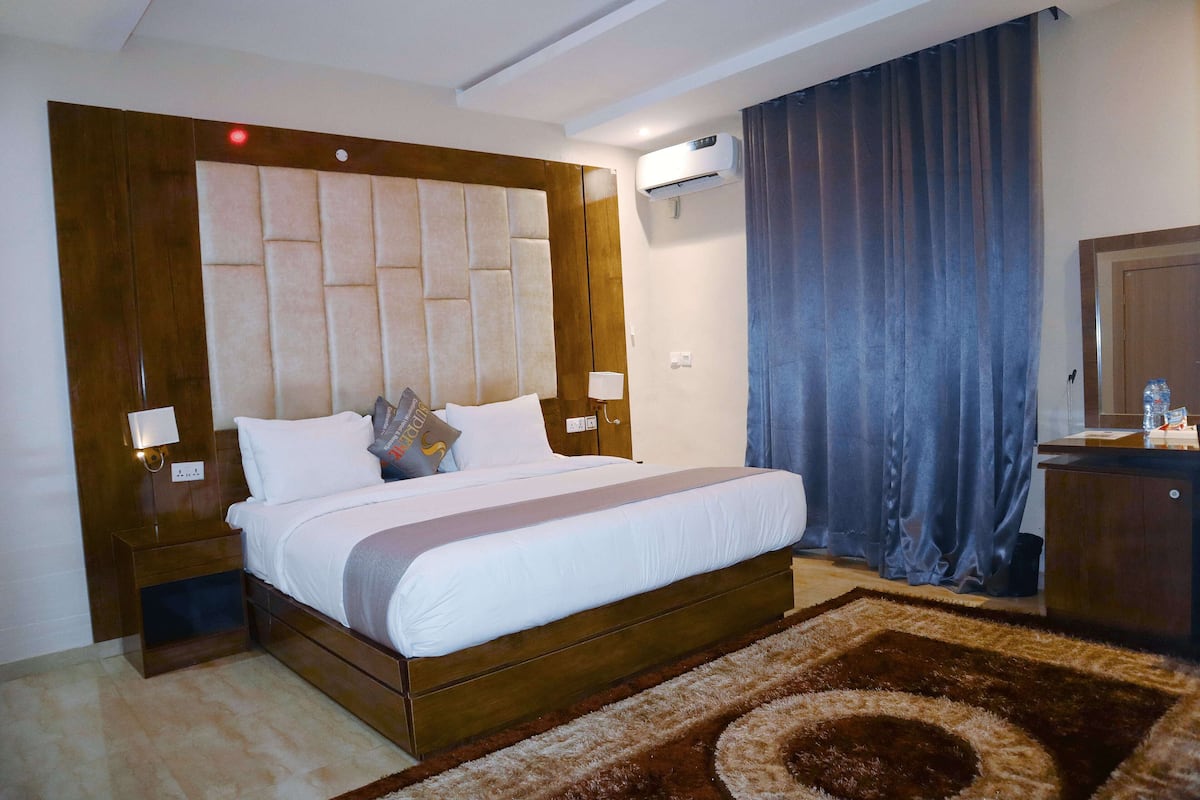 Quarto de hotel moderno com uma cama grande, cabeceira de madeira e ar condicionado integrado.
