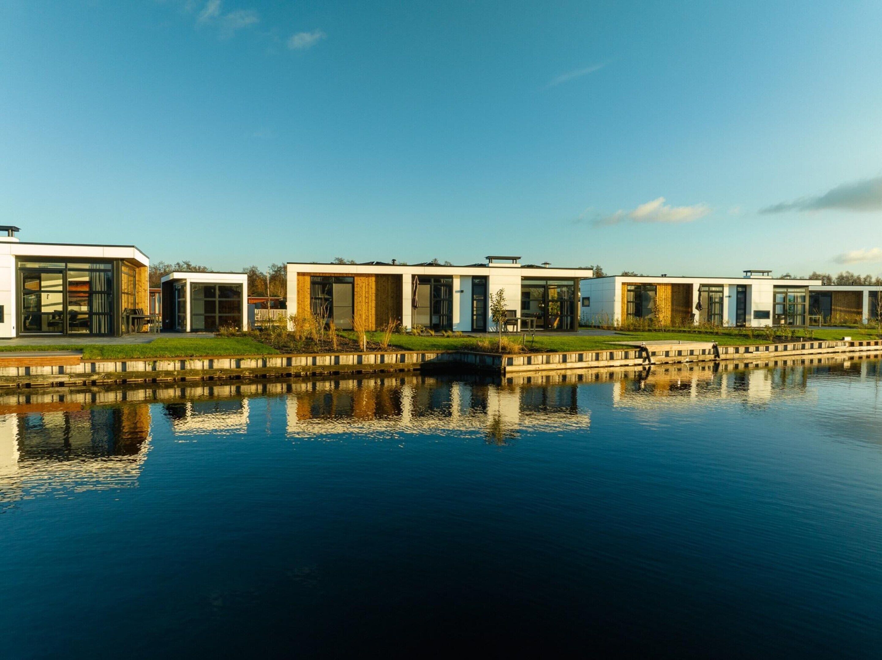 Um complexo residencial moderno com várias casas ao longo de um canal, com grandes janelas de vidro e arquitetura contemporânea.
