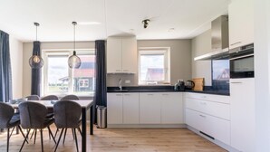 Cozinha moderna com armários brancos, bancada preta e área de refeições com mesa e cadeiras.