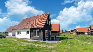Uma fileira de casas modernas com telhados de ladrilho vermelho, paredes brancas e paisagem gramada.