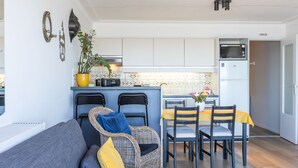 Uma sala de estar moderna com um sofá cinza, uma área de jantar com uma mesa amarela e uma cozinha com armários brancos e micro-ondas.