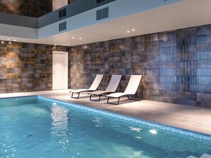 Piscina interior moderna com duas espreguiçadeiras e uma parede de pedra.