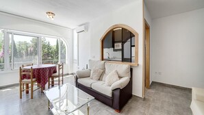 Uma sala de estar espaçosa com uma mesa de centro de vidro, um sofá e um espaço de jantar com mesa e cadeiras.