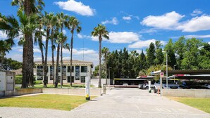 Um estacionamento com entrada gradeada, palmeiras e um edifício com placas.