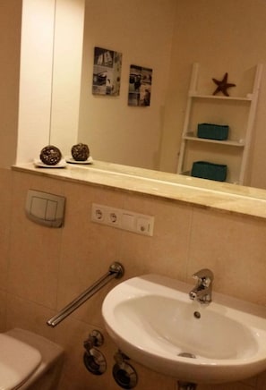 Casa de banho com pia, sanita e espelho. Existem objetos decorativos na parede e uma prateleira com uma estrela-do-mar.