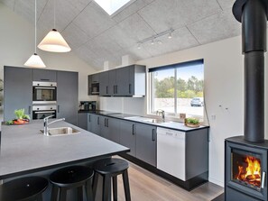Cozinha moderna com ilha central, eletrodomésticos de aço inoxidável e lareira a lenha.
