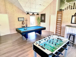 Quarto com mesa de bilhar, mesa de futebol de mesa, paredes de madeira e uma escada.