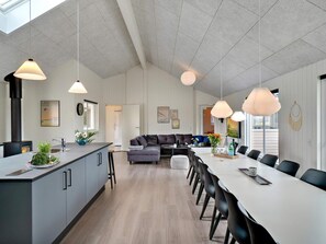 Cozinha moderna com ilha central, área de jantar com mesa comprida e cadeiras, e um espaço de estar aconchegante com sofá.