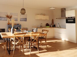 Cozinha moderna com armários de madeira, mesa de jantar com cadeiras e luminária pendente.