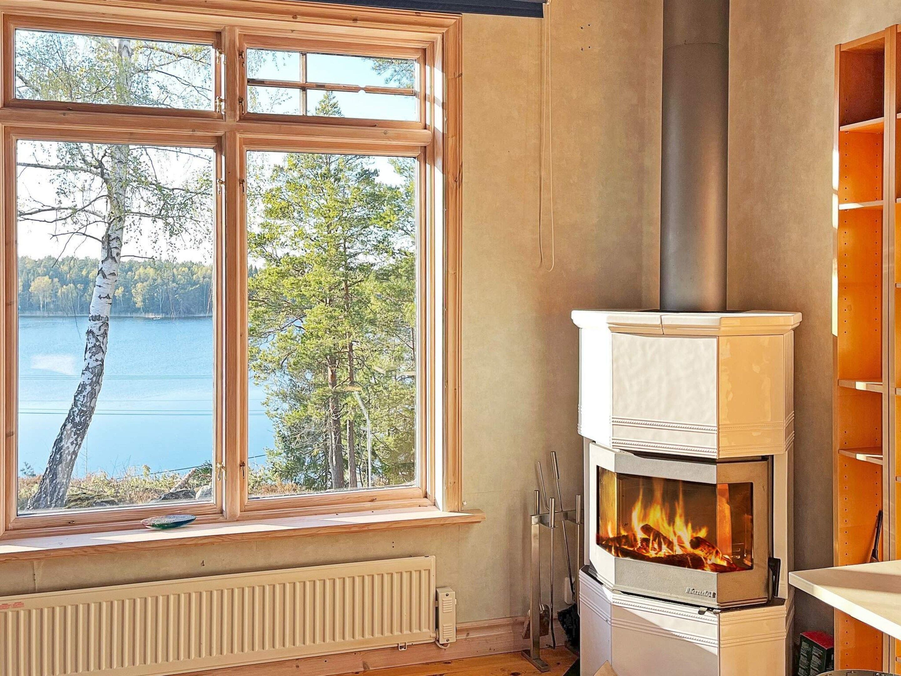 Quarto com uma grande janela com vista para um lago, uma lareira a lenha e um radiador.