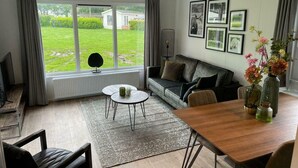 Uma sala de estar moderna com uma janela grande, um sofá, uma mesa de centro e uma mesa de jantar.