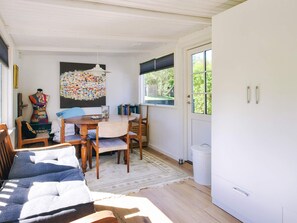 Um quarto com uma mesa de jantar, cadeiras, um sofá, uma janela com persianas, um armário branco e uma parede com colcha.