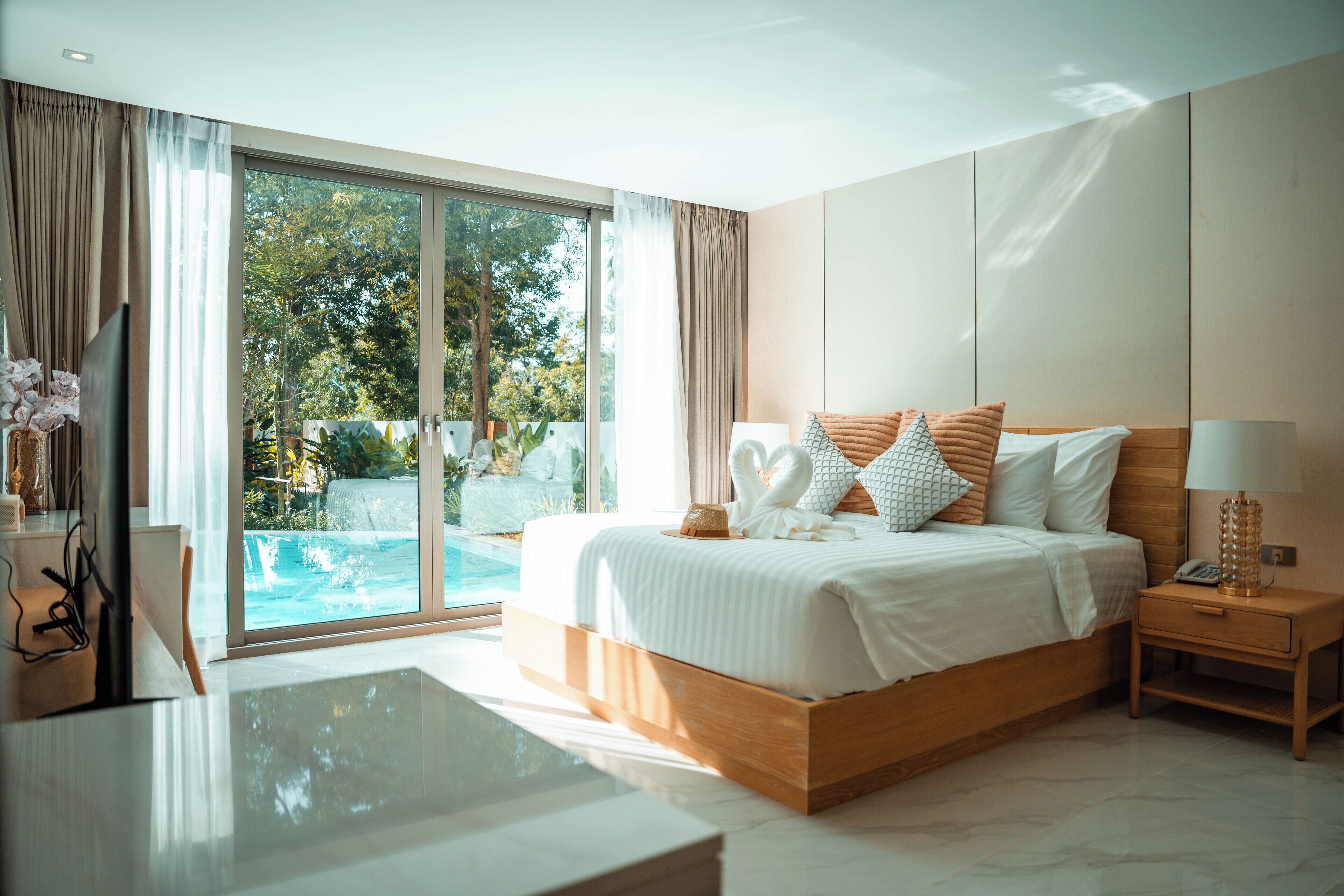 Quarto moderno com uma cama grande, uma mesa de cabeceira e vista para uma piscina.
