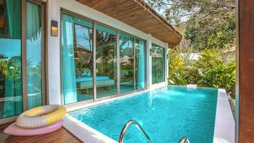 Piscina com deck de madeira, sala envidraçada com porta deslizante e vista para o verde ao redor.