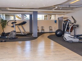 Uma academia com equipamentos de exercícios, esteira, bicicleta ergométrica e remo.