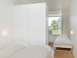Quarto com duas camas, janela com vista para árvores e varanda com grades.