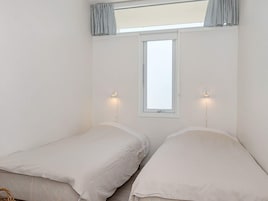 Quarto com duas camas de solteiro, uma janela com cortinas e duas luminárias de parede para leitura.