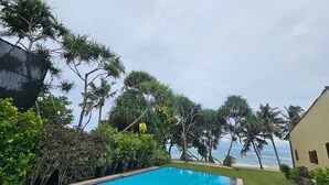 Piscina com vista para o oceano, rodeada por vegetação tropical e um edifício.
