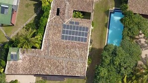 Vista aérea de uma propriedade à beira-mar, com piscina, painéis solares e palmeiras.