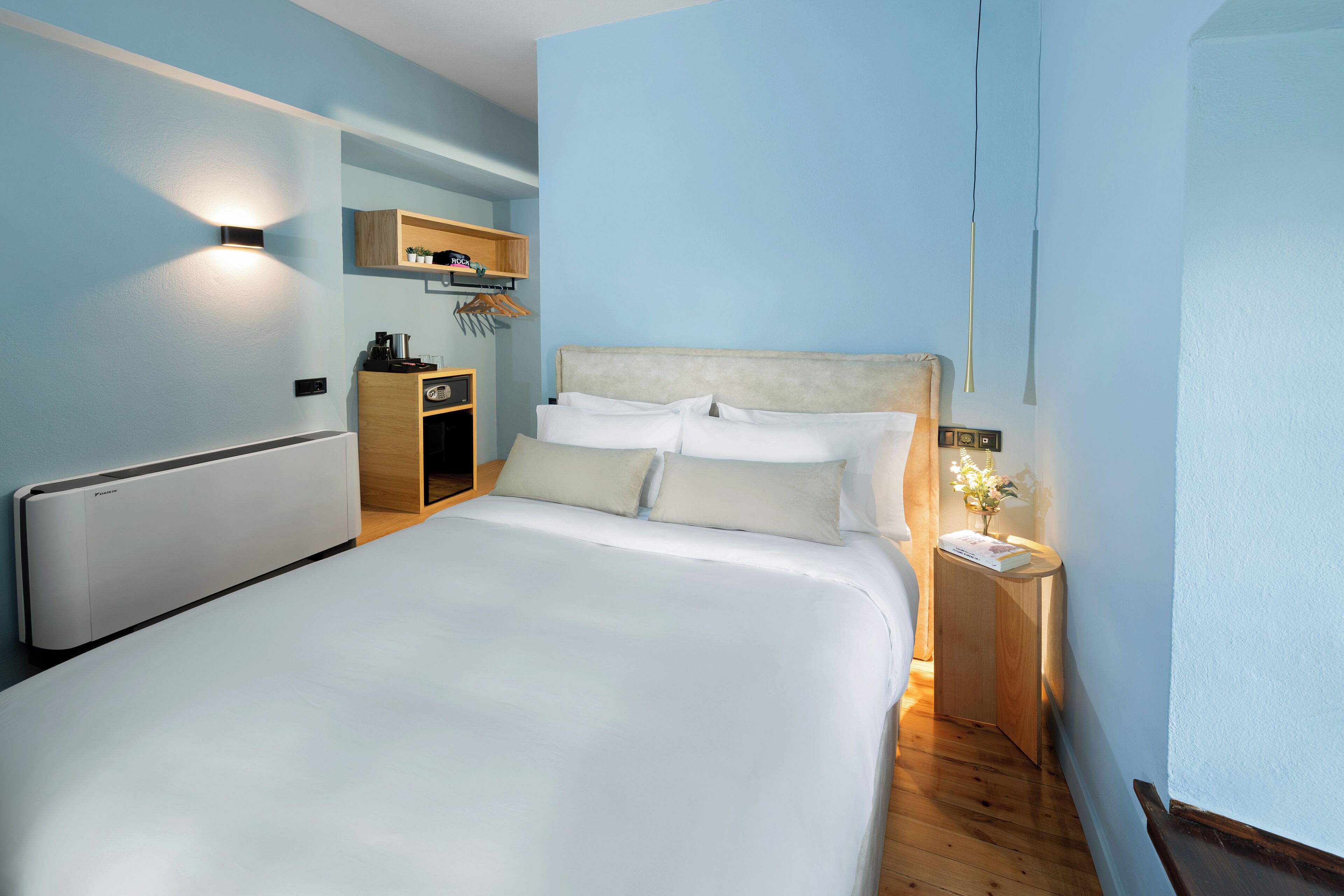 Quarto moderno com uma cama grande, uma mesa de cabeceira com abajur, cômoda de madeira e prateleira na parede.