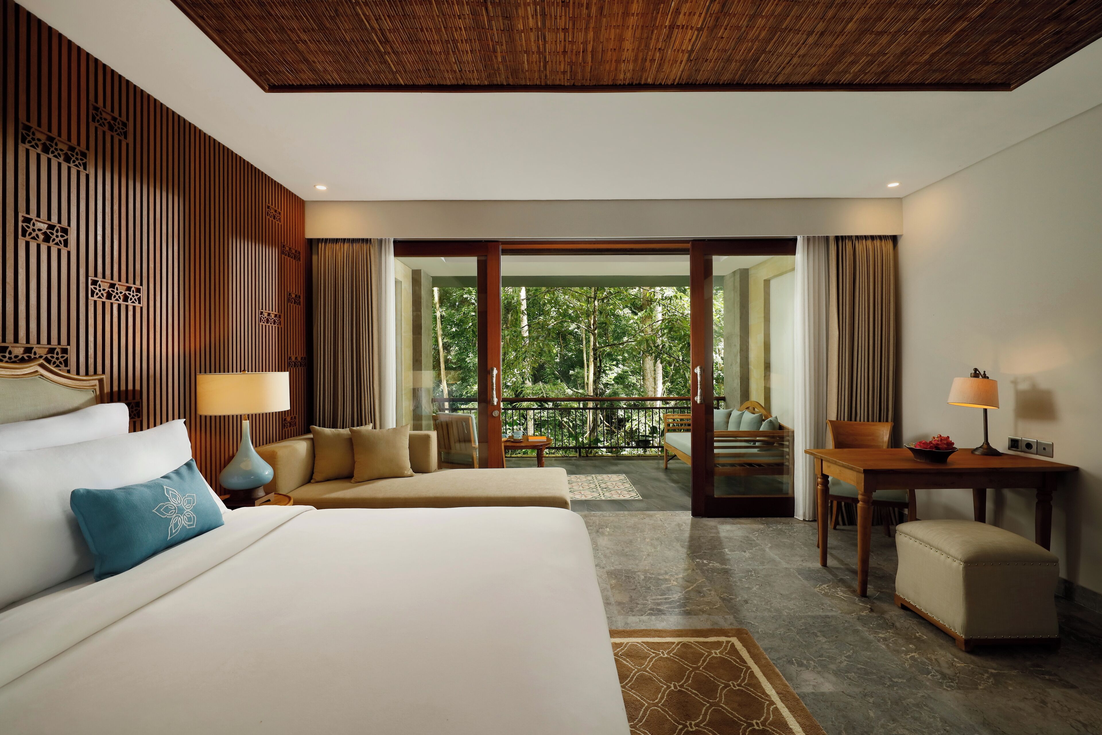 Quarto de hotel com uma cama grande, sofá, escrivaninha e varanda com vista para árvores.
