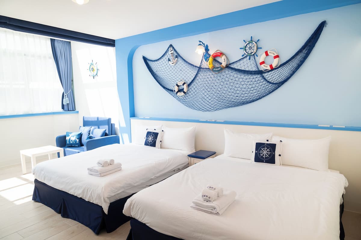 Quarto de hotel com duas camas, uma escrivaninha, uma cadeira e uma grande decoração de parede com elementos náuticos.