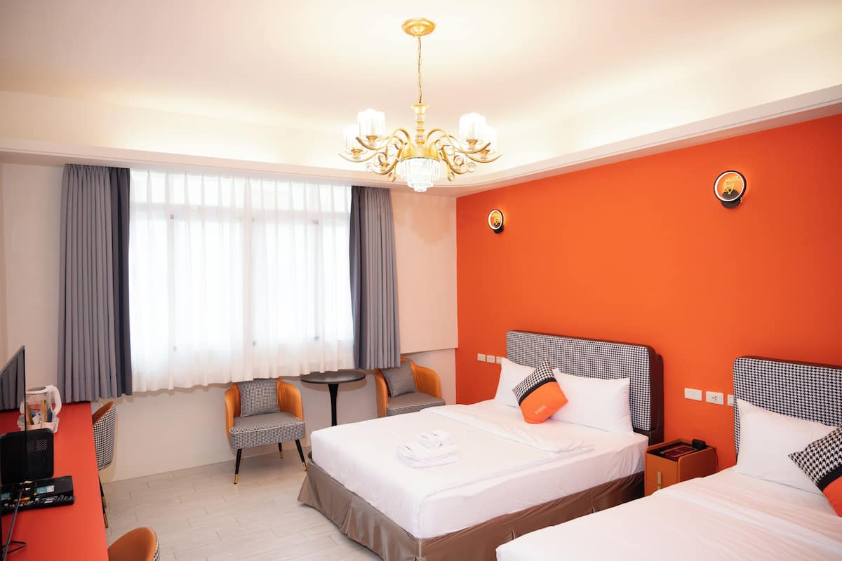 Quarto de hotel com duas camas, uma escrivaninha, uma cadeira, uma mesinha e um candelabro.