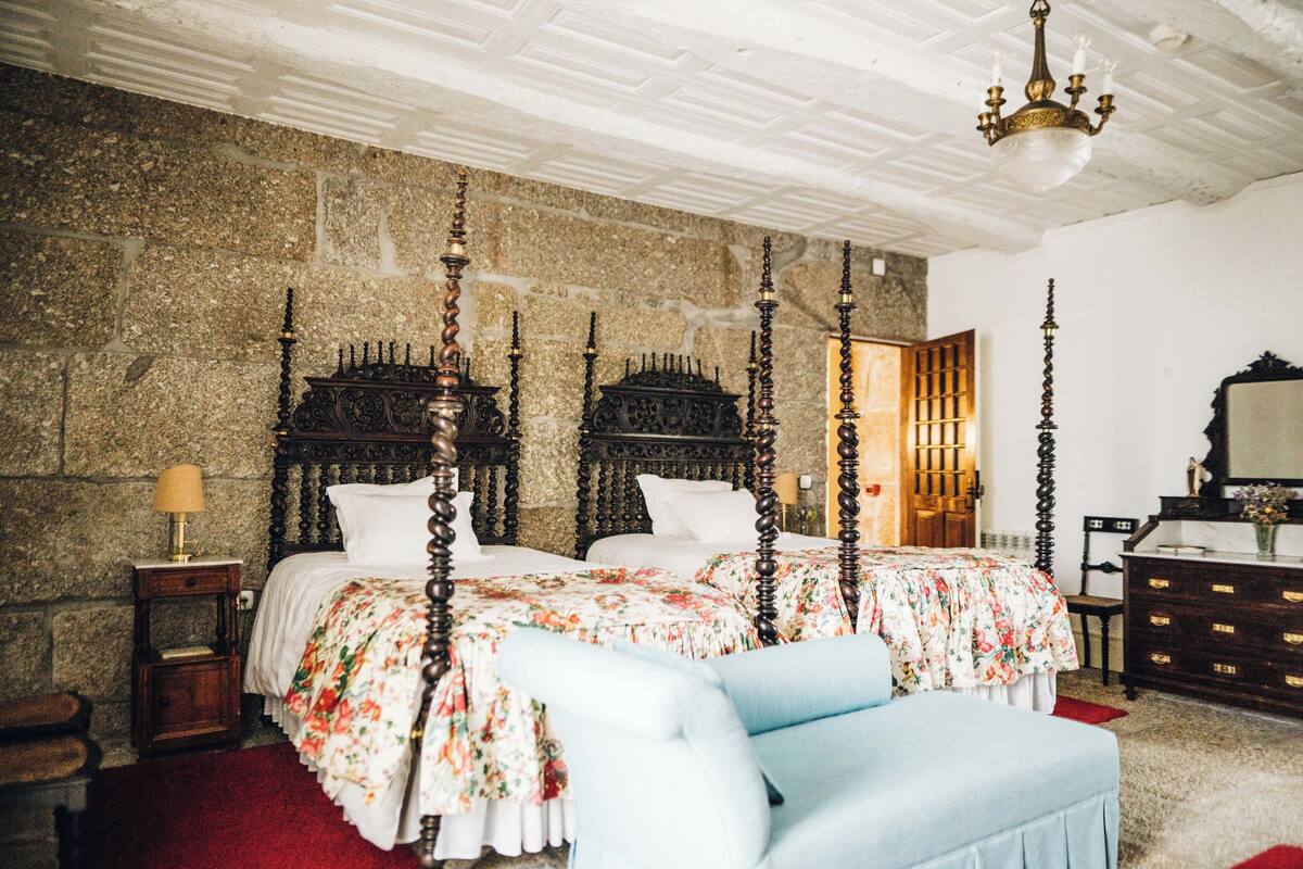 Quarto com parede de pedra, cama de dossel de madeira, cômoda de madeira e um candelabro.