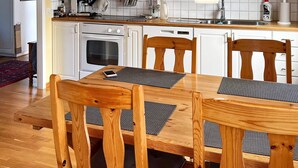 Uma sala de jantar com uma mesa e cadeiras de madeira, uma cozinha ao fundo e um tapete vermelho no chão.