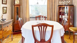 Uma sala de jantar com uma mesa redonda, cadeiras, um candelabro, um relógio e uma menora.