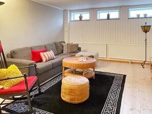 Uma sala de estar com sofá cinza, mesa de centro de vime redonda, tapete estampado e luminária de chão.