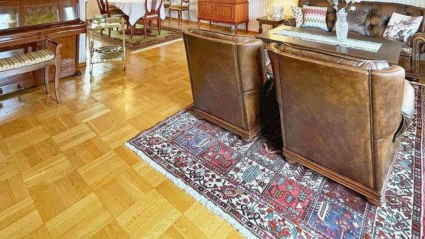 Uma sala de estar ampla com um piano, poltronas de couro, uma mesa de jantar e um tapete estampado.