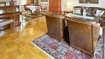 Uma sala de estar ampla com um piano, uma mesa de jantar com cadeiras, um sofá e um tapete estampado.