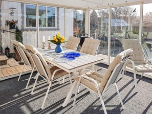 Uma sala de sol com mesa e cadeiras, amplas janelas e vista para o exterior.