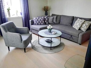 Sala de estar com sofá cinza, poltrona cinza e mesa de centro redonda com um vaso de flores.