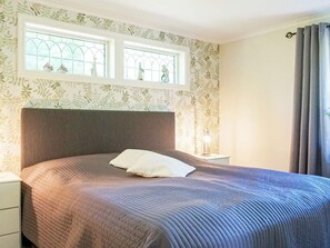 Quarto com cama, mesa de cabeceira, janela com painéis decorativos e cortina.