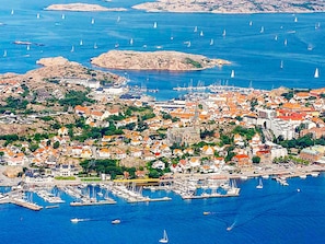 Uma vila costeira com um porto cheio de barcos, rodeada por edifícios residenciais com telhados vermelhos.