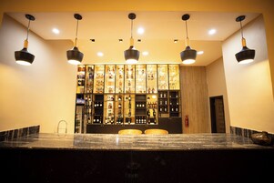 Uma área de bar com bancada de mármore, várias luminárias pendentes e prateleiras repletas de garrafas.