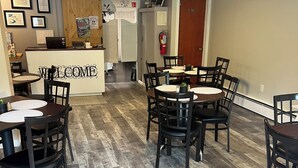Uma área de refeições com várias mesas e cadeiras, uma mesa de recepção e um letreiro com a palavra 'WELCOME'.